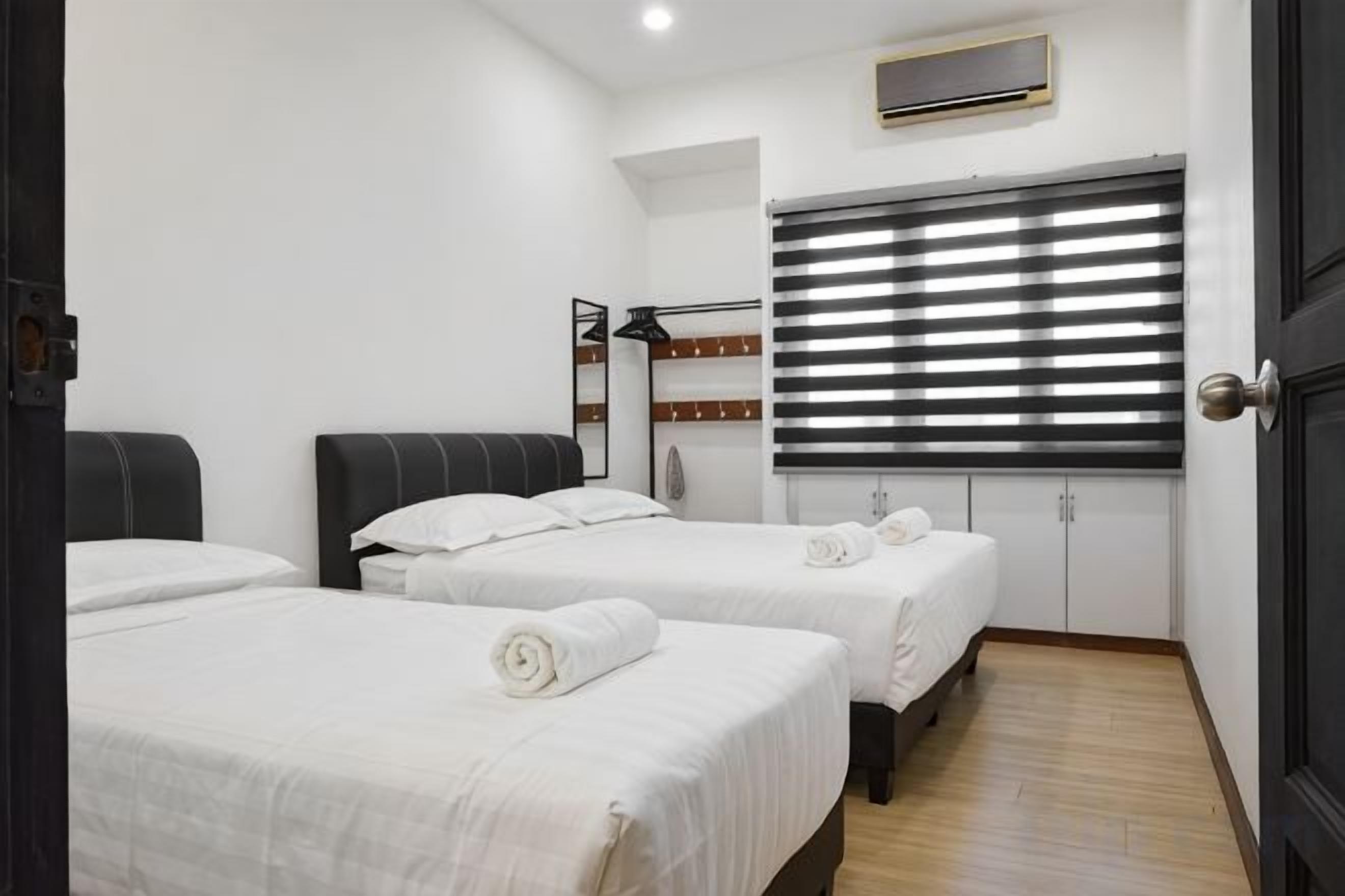 Quarto de hotel com duas camas, um guarda-roupa, uma janela com persianas e uma porta.