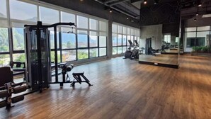 Uma academia espaçosa com grandes janelas, diversos equipamentos de ginástica e piso de madeira.