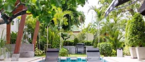 Piscina com espreguiçadeiras, cercada por vegetação e um pergolado.
