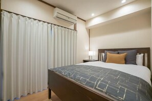 Quarto de hotel com cama, cortinas, ar condicionado, mesa de cabeceira e luminária.