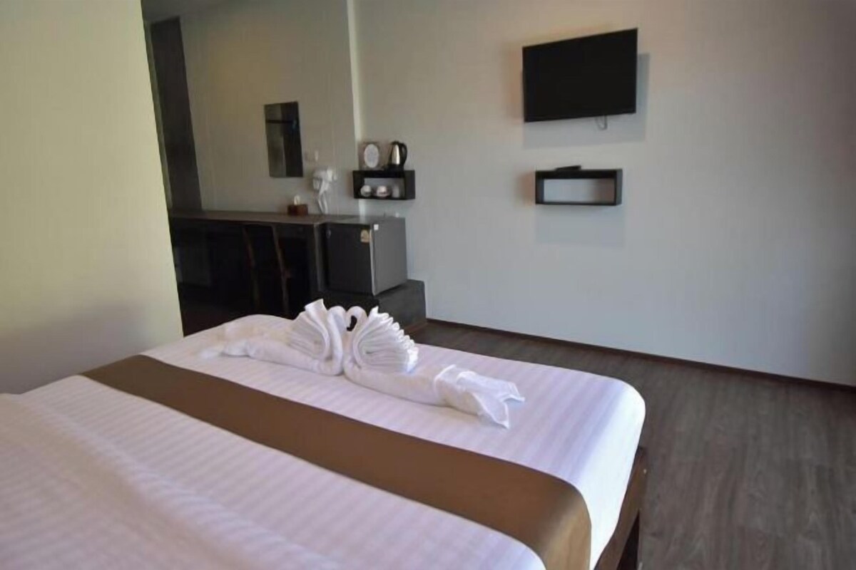 Quarto de hotel com cama bem arrumada, televisão de tela plana na parede e pequena mesa de trabalho com cadeira.