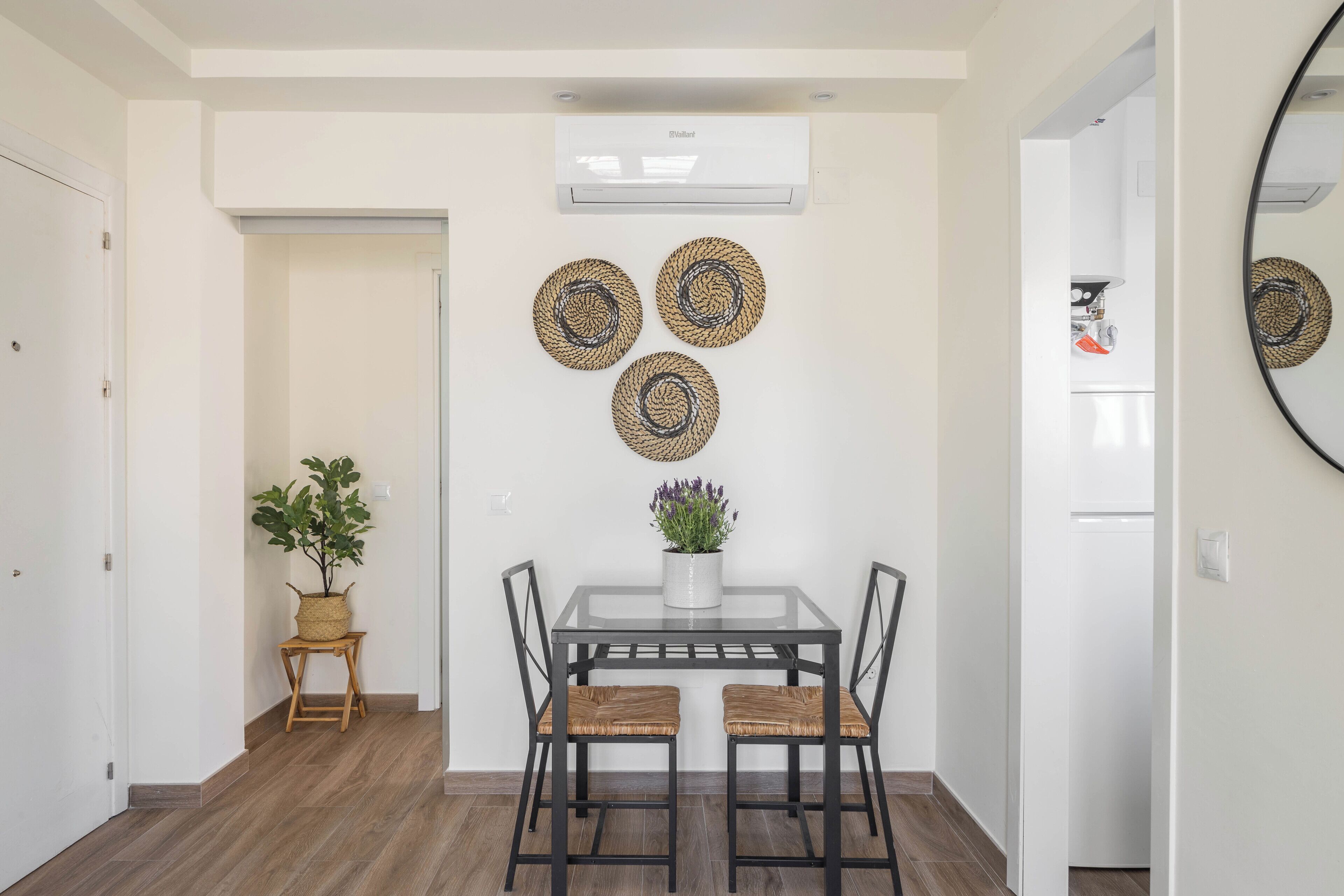 Uma área de refeições com uma mesa de vidro, duas cadeiras e um vaso com planta.