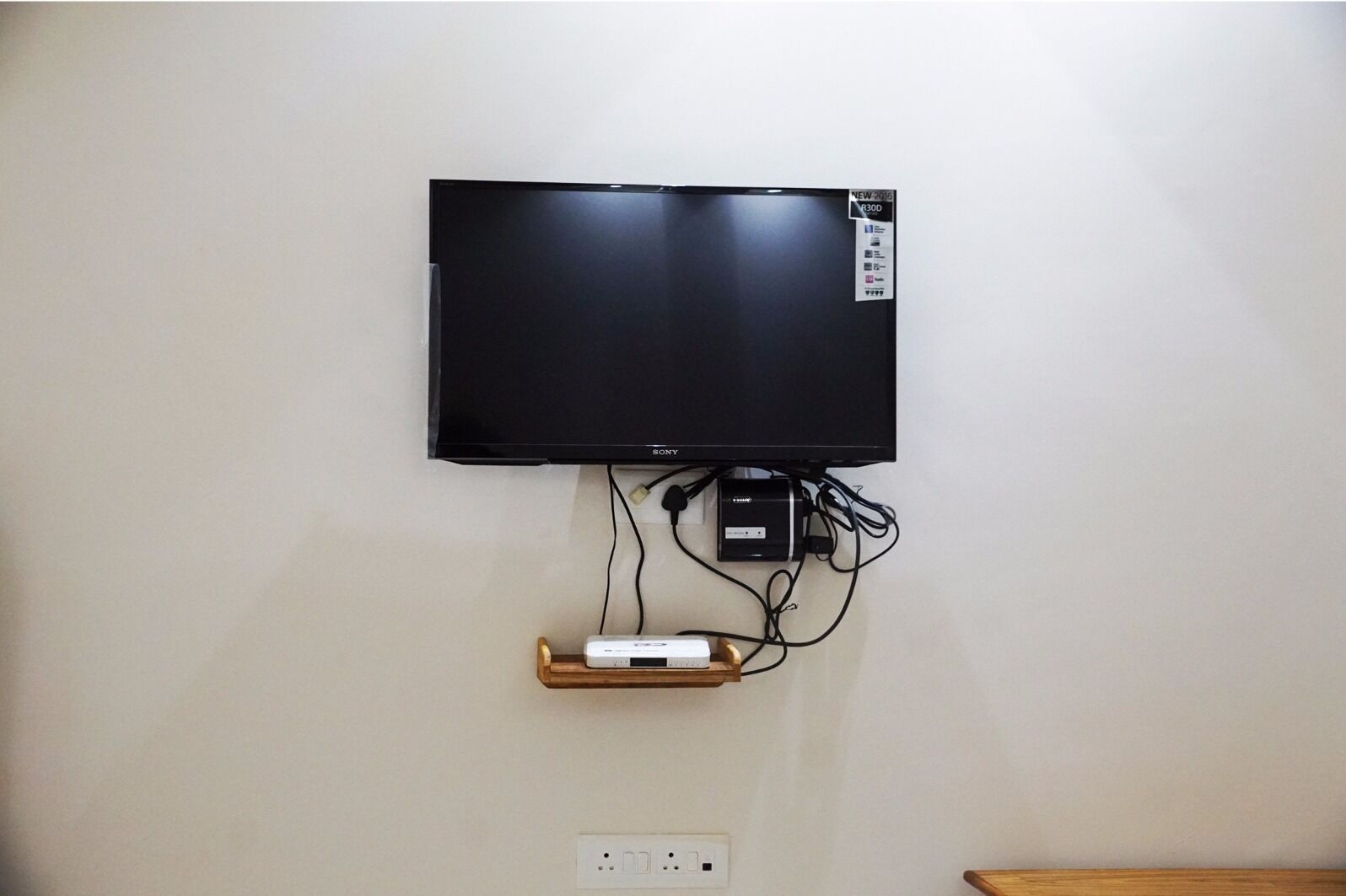 Televisão de tela plana fixada na parede, com um filtro de energia e cabos abaixo.