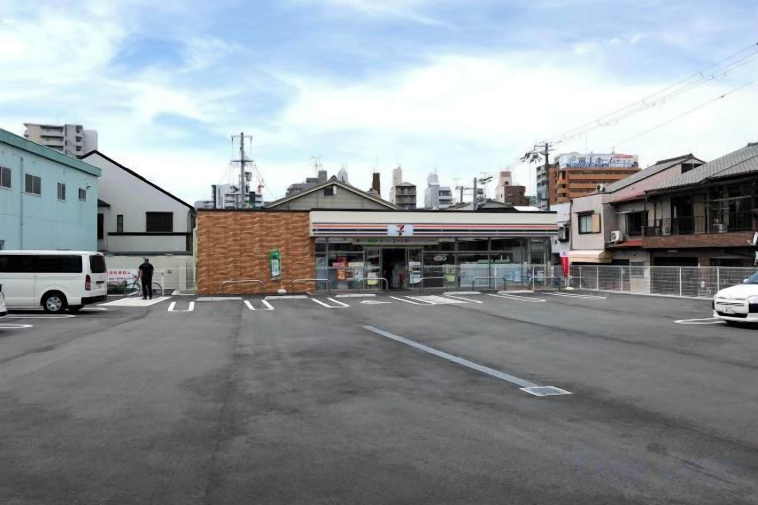 Estacionamento com um edifício ao fundo, uma van branca e uma pessoa caminhando.
