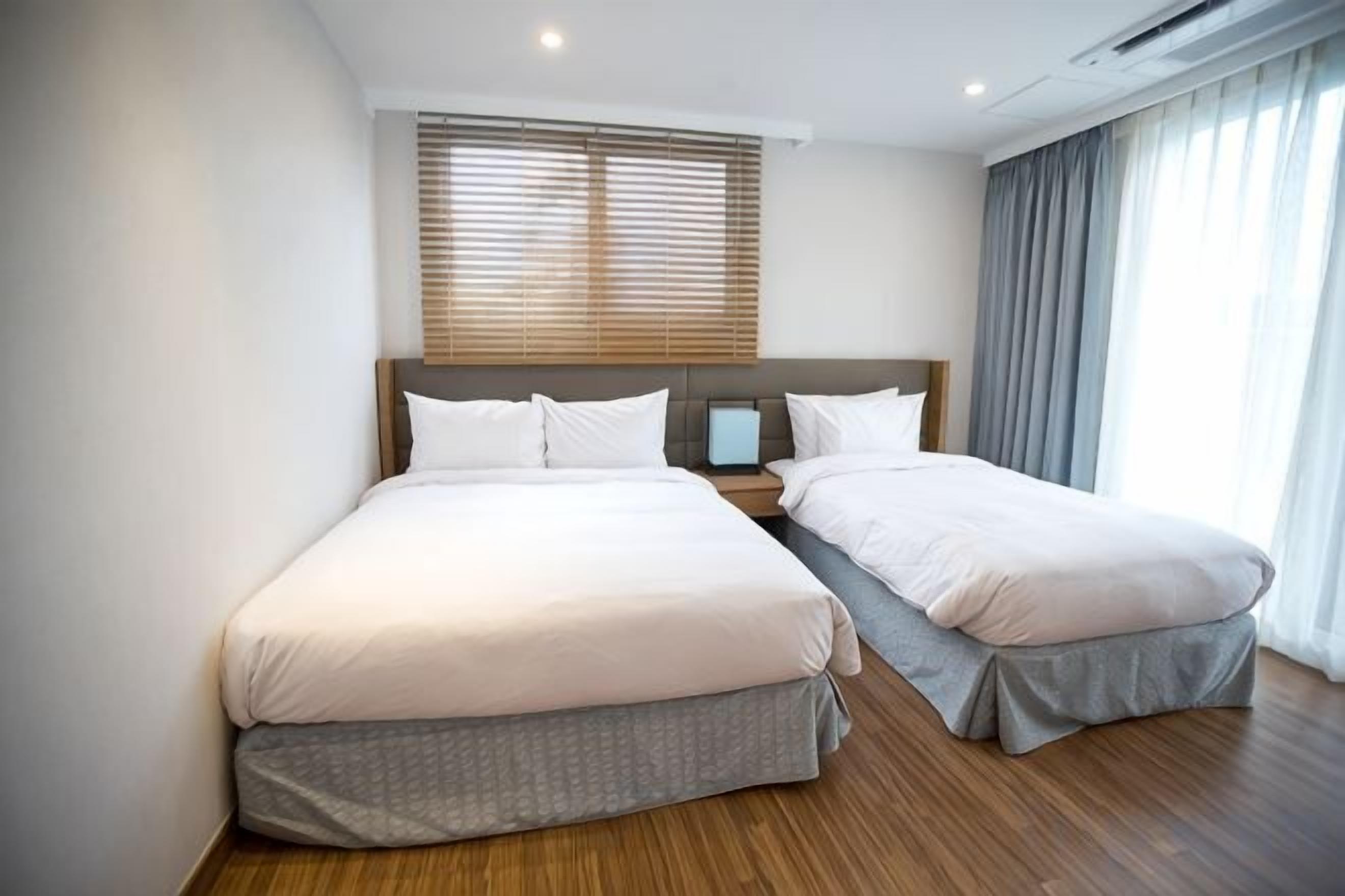 Quarto de hotel com cama de casal, mesas de cabeceira, cabeceira e janela com cortinas.