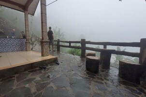 Uma área pavimentada em pedra com grade de madeira, plataforma e vista para uma paisagem enevoada.