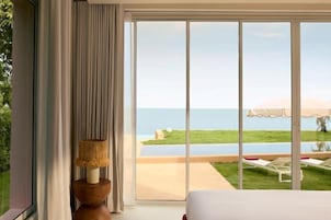 Quarto com uma grande porta de correr de vidro que dá para uma área à beira da piscina e vista para o mar.