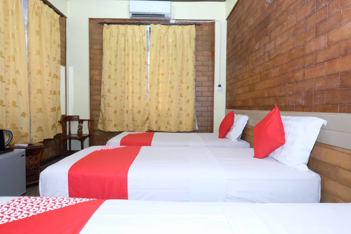 Quarto de hotel com duas camas, parede de tijolos, janela com cortinas, escrivaninha com abajur e um pequeno frigorífico.