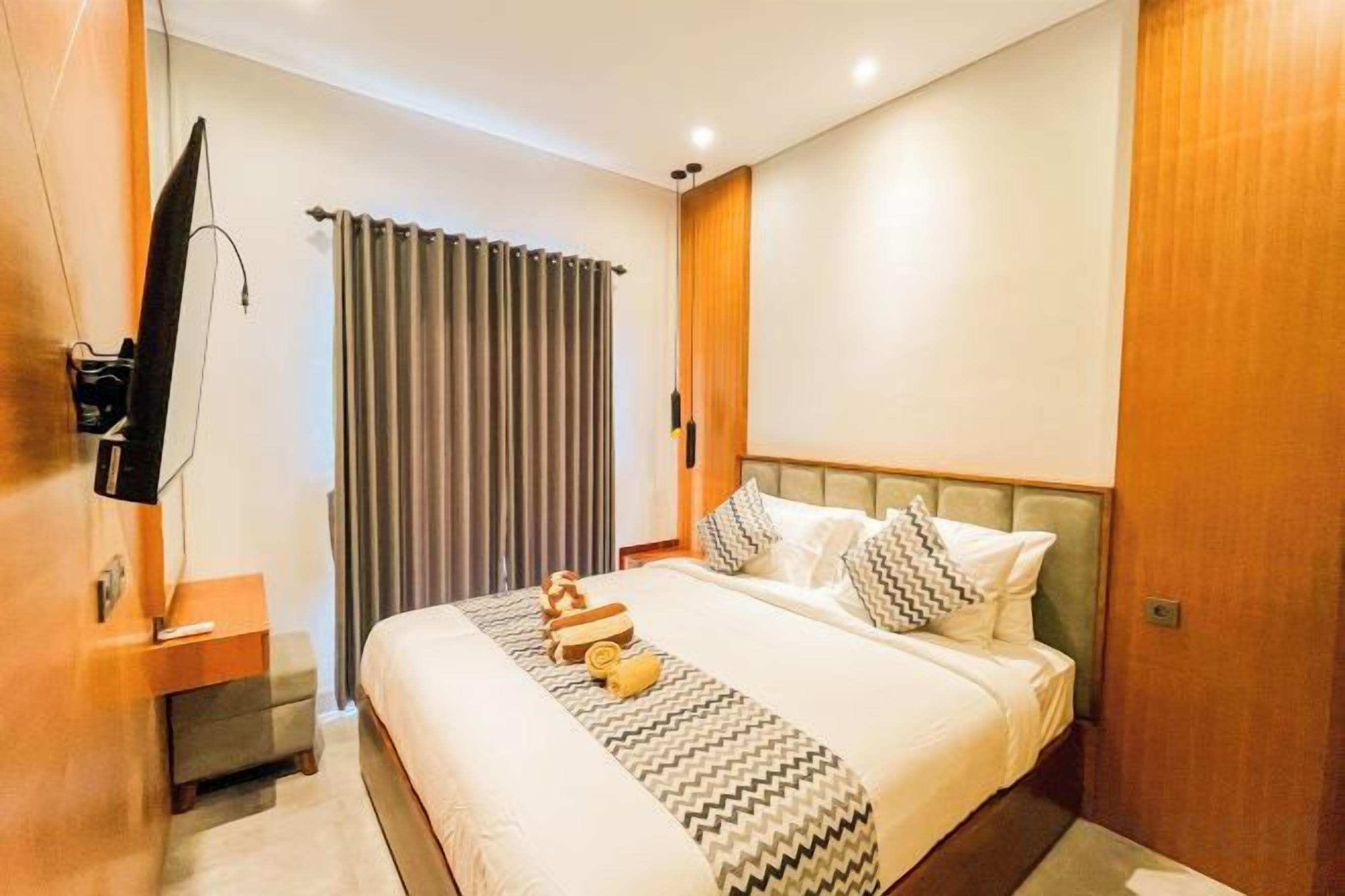 Quarto de hotel com cama, cortinas, televisão e porta de madeira.