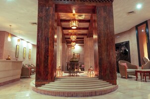 Um hall de entrada com balcão de atendimento, área de estar e uma fonte decorativa central.