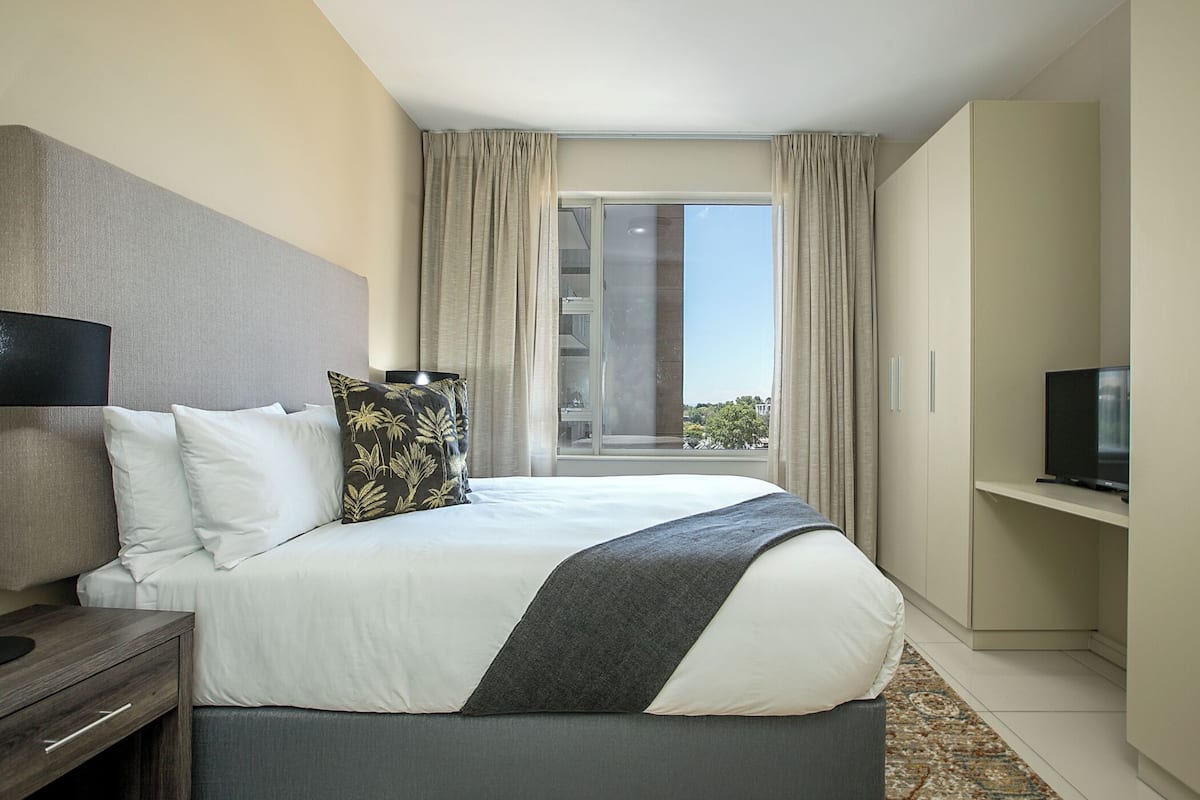 Quarto de hotel com uma cama grande, televisão, escrivaninha e janela com cortinas.
