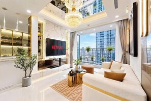 Uma sala de estar moderna com uma grande televisão de tela plana, um sofá, um lustre e vista para uma varanda.