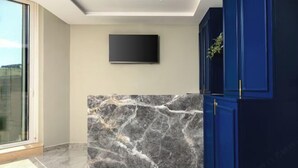 Uma área de recepção moderna com balcão de mármore, televisão de tela plana e armários azuis.