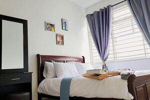 Quarto com cama, mesa de cabeceira, janela com cortinas e decoração na parede.