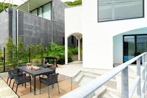 Um pátio externo com mesa e cadeiras de jantar, rodeado por vegetação e uma estrutura de prédio moderna.
