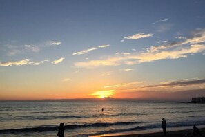 Cena de praia com o sol se pondo sobre o oceano.