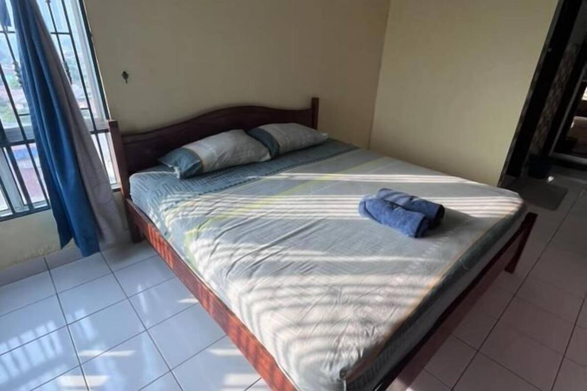 Uma cama de solteiro num quarto com janela, cortina e chão em mosaico.