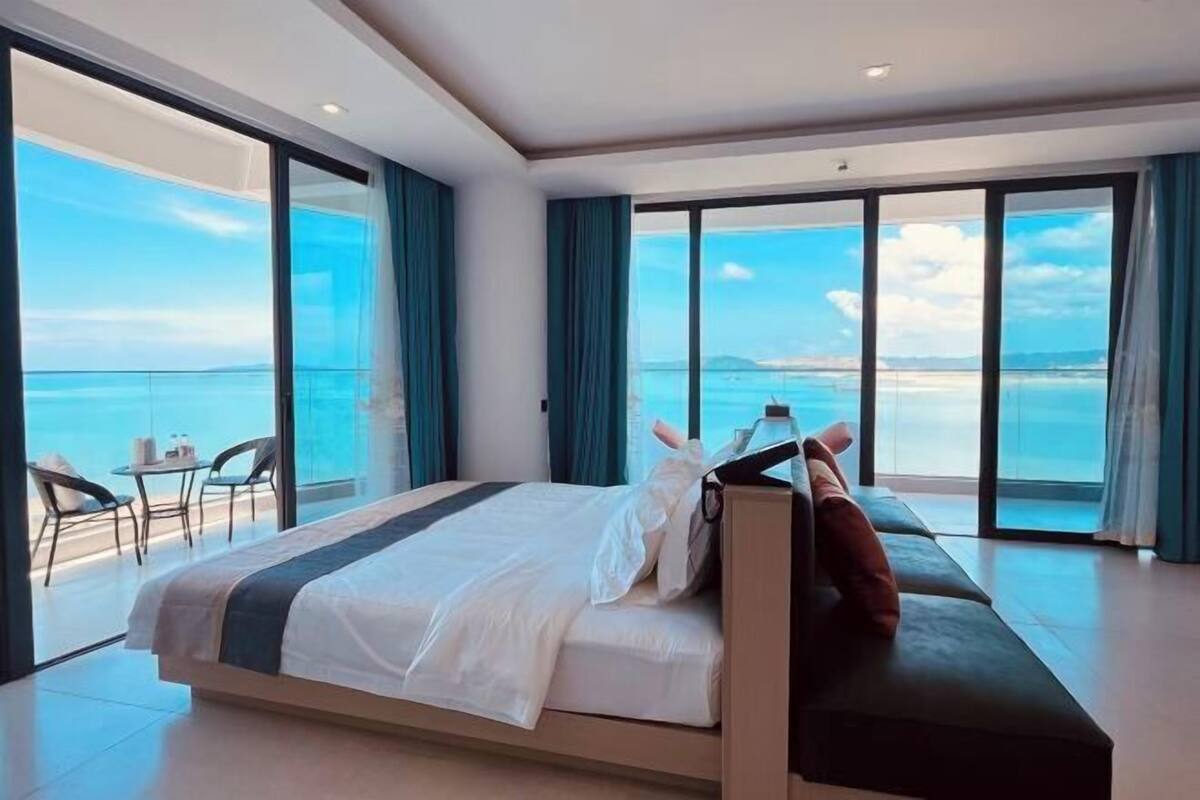 Quarto de hotel moderno com uma cama grande, um sofá e uma varanda com vista para o mar.