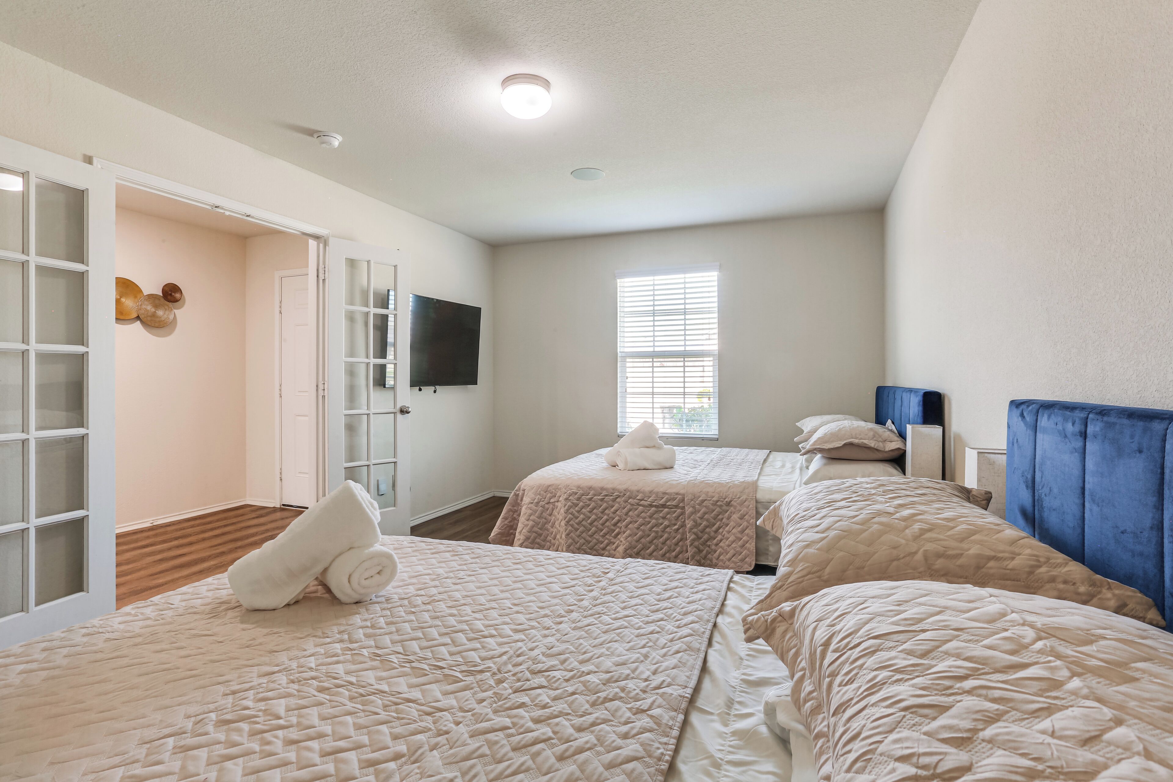 Quarto de hotel com duas camas, televisão e janela com persianas.