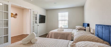 Quarto de hotel com duas camas, televisão e janela com persianas.