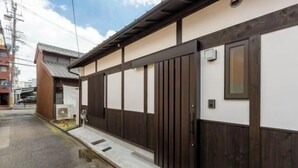 Um edifício japonês tradicional com porta de madeira, um pequeno aparelho de ar condicionado e céu claro.