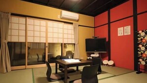 Um quarto japonês tradicional com tatames, uma porta deslizante estilo shoji, uma televisão e uma parede com destaque em vermelho.