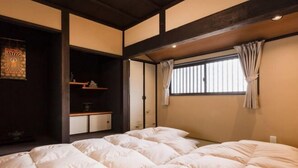 Quarto em estilo japonês tradicional com tatames, teto de madeira baixo e uma cama grande com roupa de cama branca.