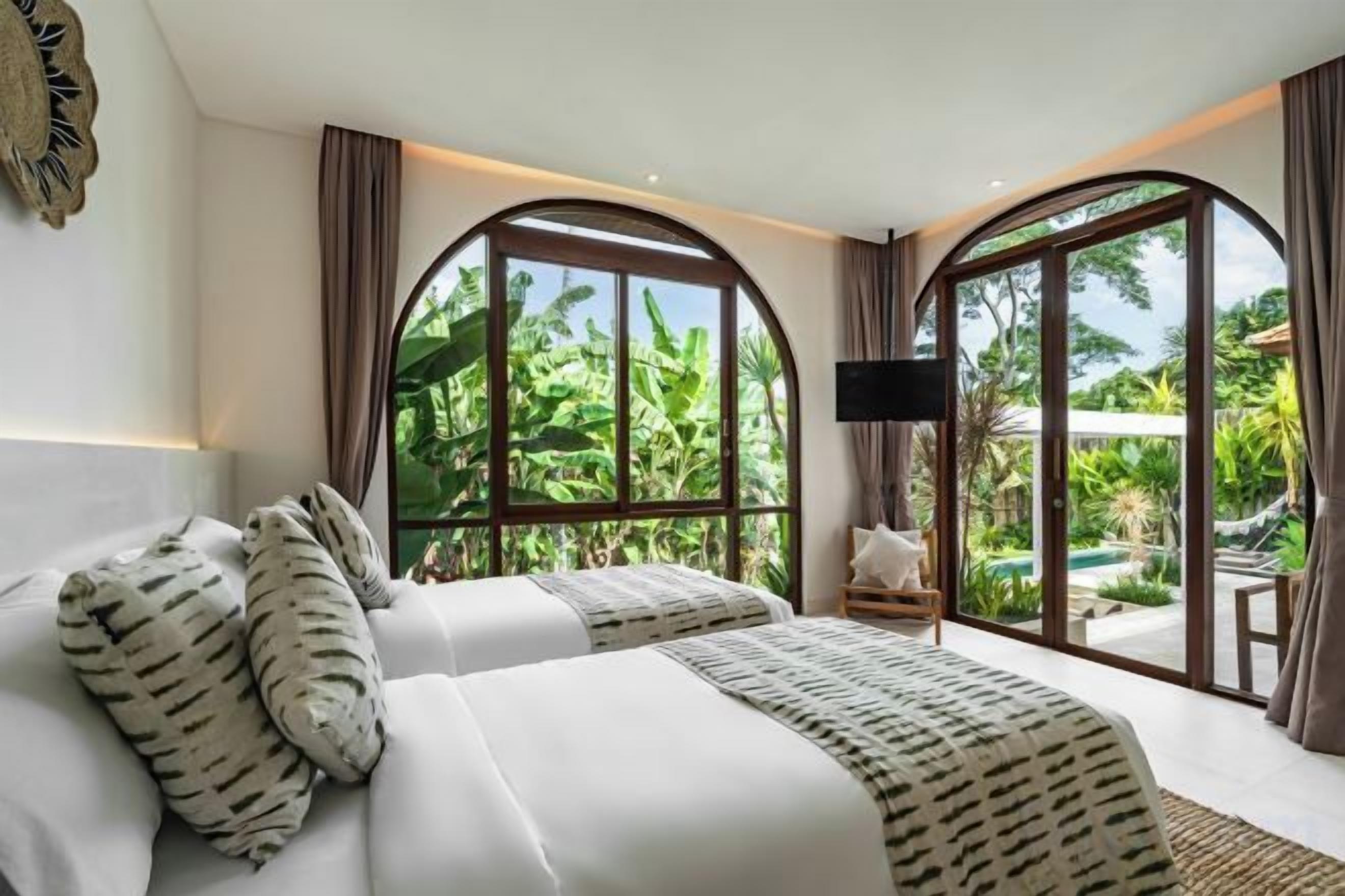 Quarto com cama grande, televisão e vista para um jardim através de uma porta de vidro.