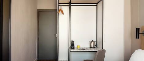 Quarto de hotel com cama, escrivaninha, cadeira, cafeteira e luminária pendente.