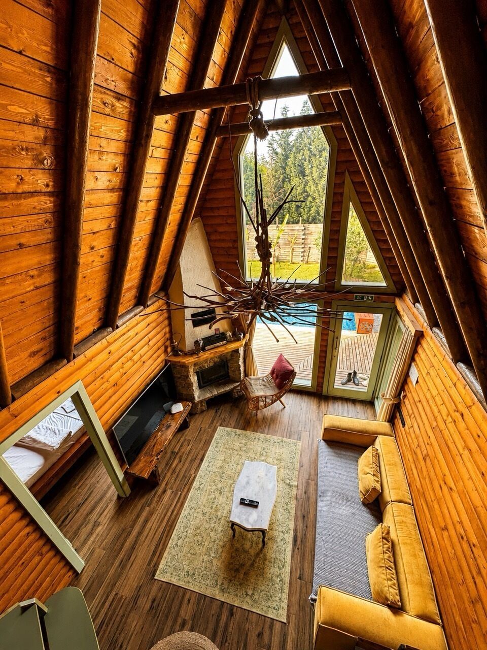 Interior de uma cabana de madeira com um quarto no mezanino, área de refeições e vista para o exterior.