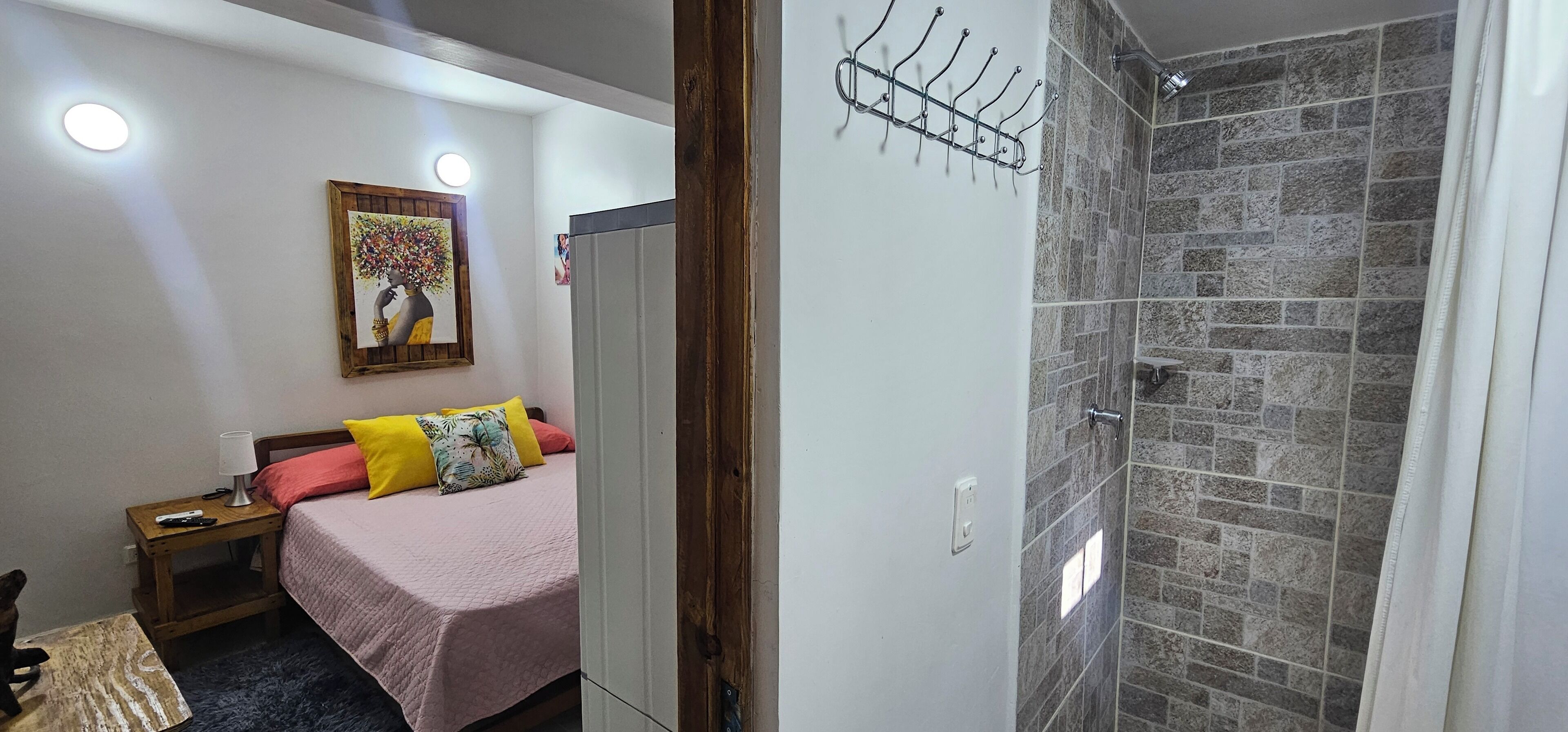 Quarto com cama, mesa de cabeceira, luminária, obra de arte na parede e área de chuveiro com parede de tijolos.