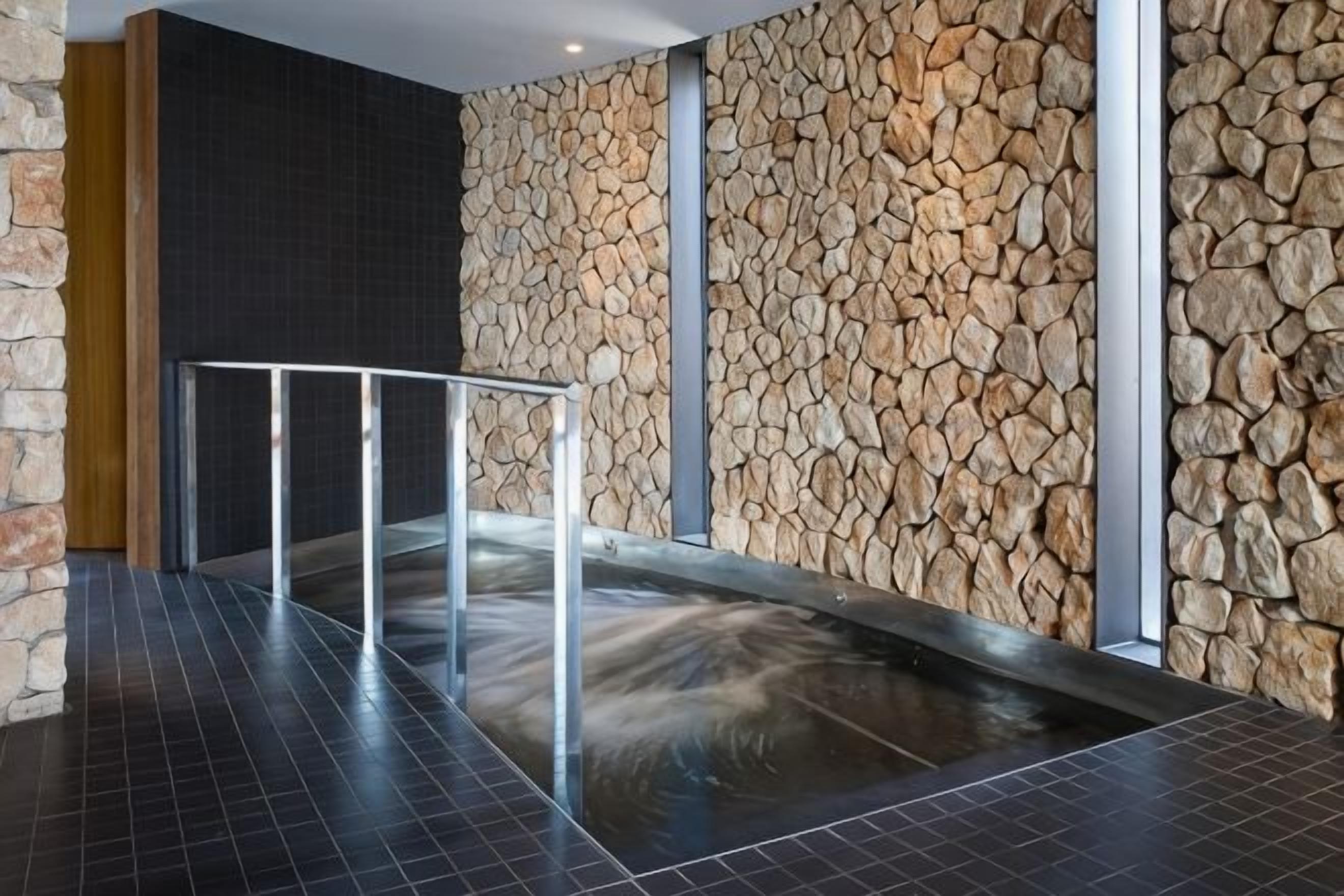 Uma área de spa com parede de pedra, guarda-corpo de metal e piso ladrilhado em preto.