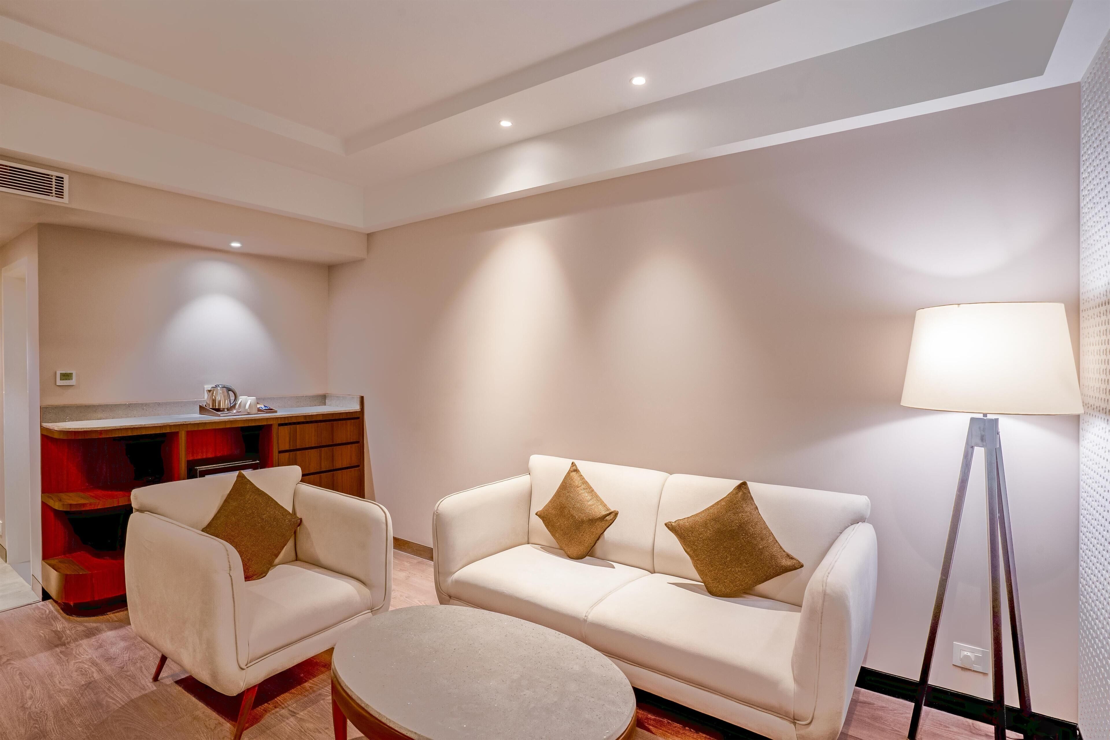 Uma sala de estar moderna com um sofá branco, duas poltronas, uma mesa de centro e um abajur.