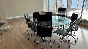 Sala de conferência com mesa de vidro e cadeiras de escritório pretas, grandes janelas e piso de madeira.