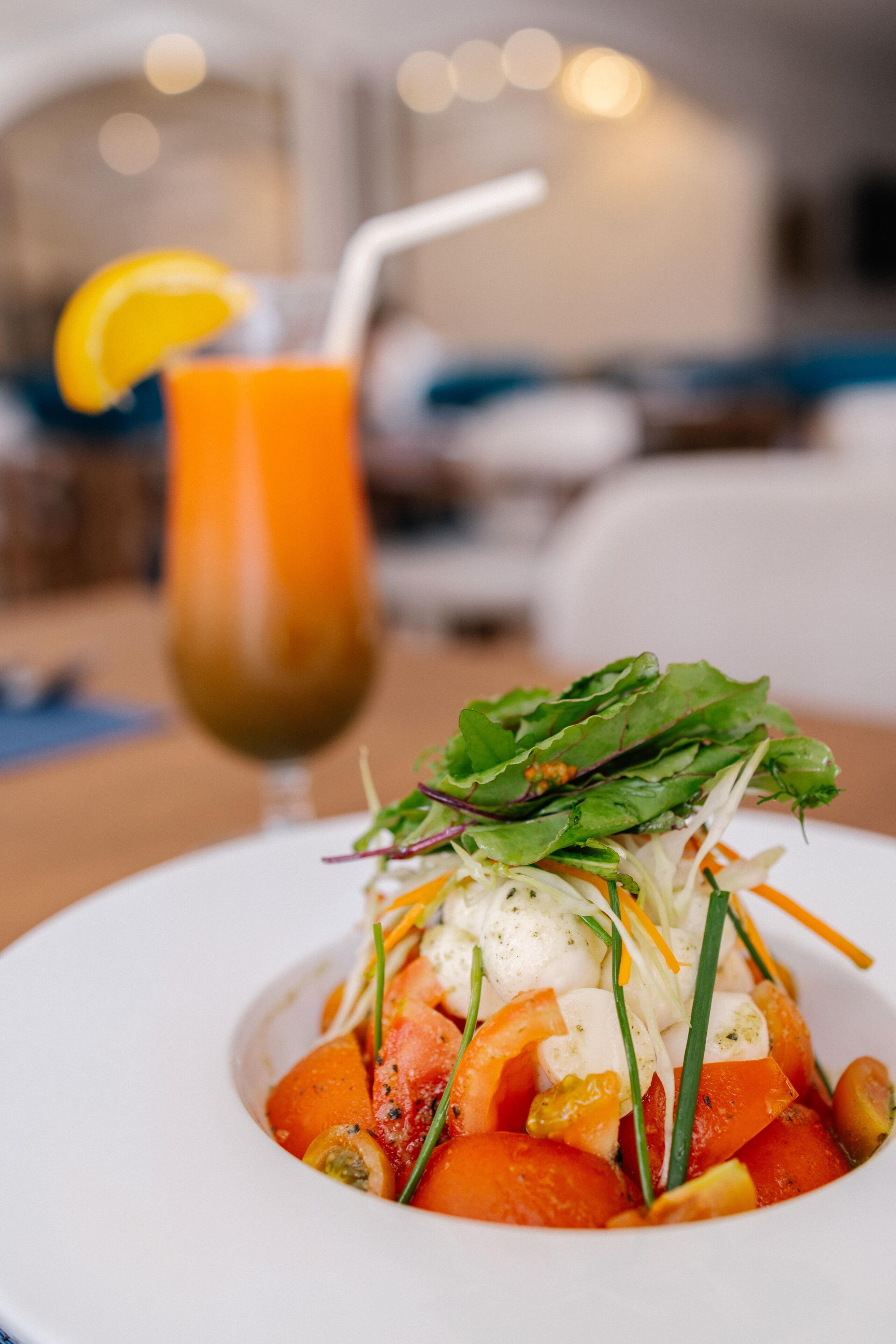 Um prato branco com salada, um copo de suco de laranja e uma fatia de limão.