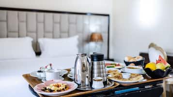 Bandeja de café da manhã com café, pães e frutas sobre a mesa de um quarto de hotel.