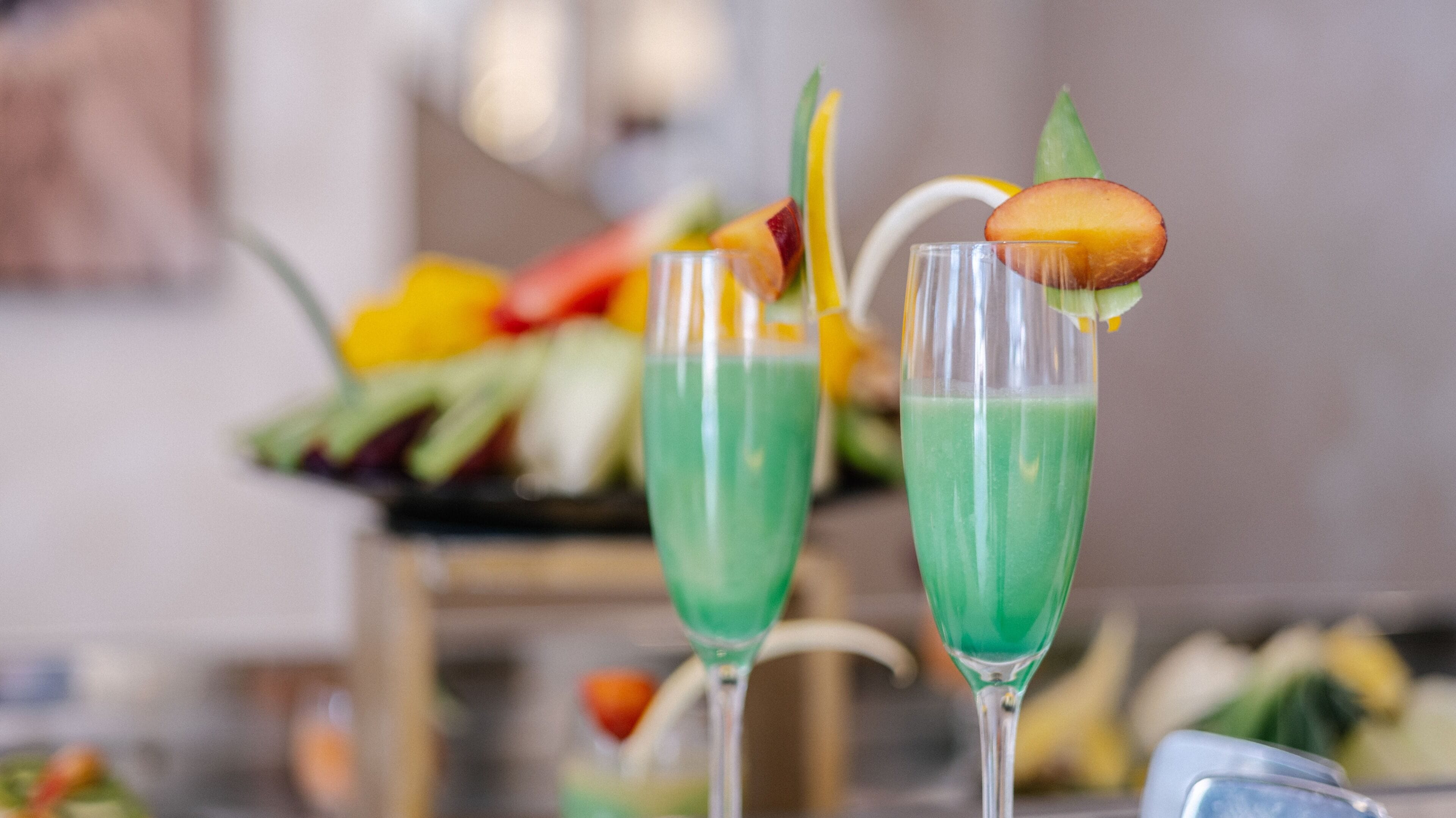 Duas bebidas verdes com guarnições de frutas sobre uma mesa.