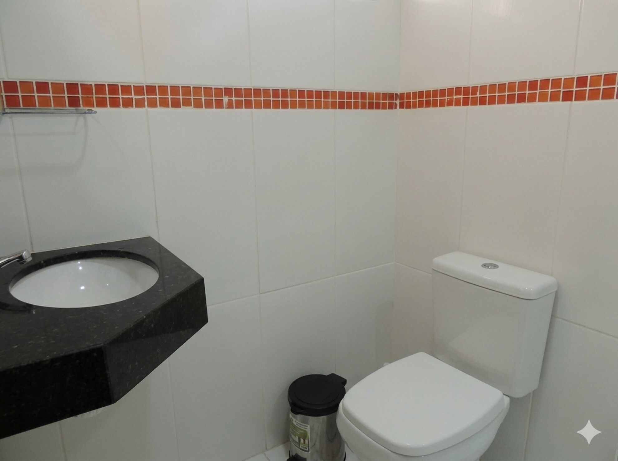 Casa de banho com lavatório preto, sanita branca e um contentor de lixo.