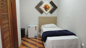Quarto pequeno e bem organizado, com uma cama, um frigorífico branco e uma porta de madeira.