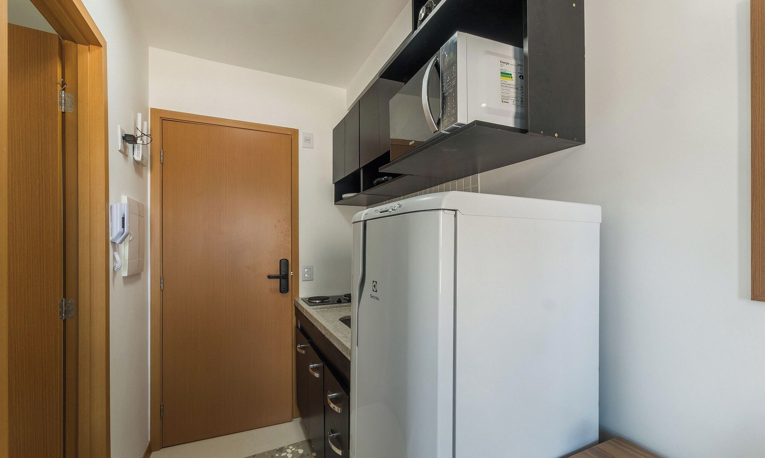 Uma cozinha compacta com micro-ondas, geladeira e porta de madeira.