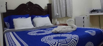 Quarto de hotel com cama, cabeceira de madeira, colcha azul estampada, travesseiros brancos e toalha branca na cama.
