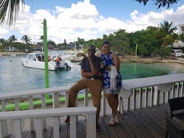 Um casal em um deck de madeira com vista para um porto com barcos e palmeiras.