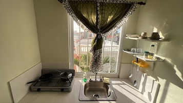 Uma cozinha compacta com fogão a gás, pia e janela com vista para prédios.