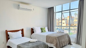 Quarto de hotel com duas camas, uma janela grande e vista, e um aparelho de ar condicionado.