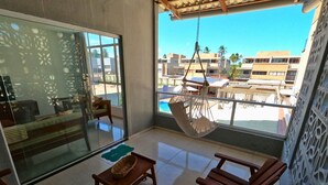 Quarto moderno com porta de vidro, cadeira suspensa, mobiliário de madeira e vista para uma piscina e edifícios.