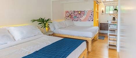 Quarto com duas camas, piso de madeira, parede com pintura floral e uma pequena escrivaninha com uma planta.
