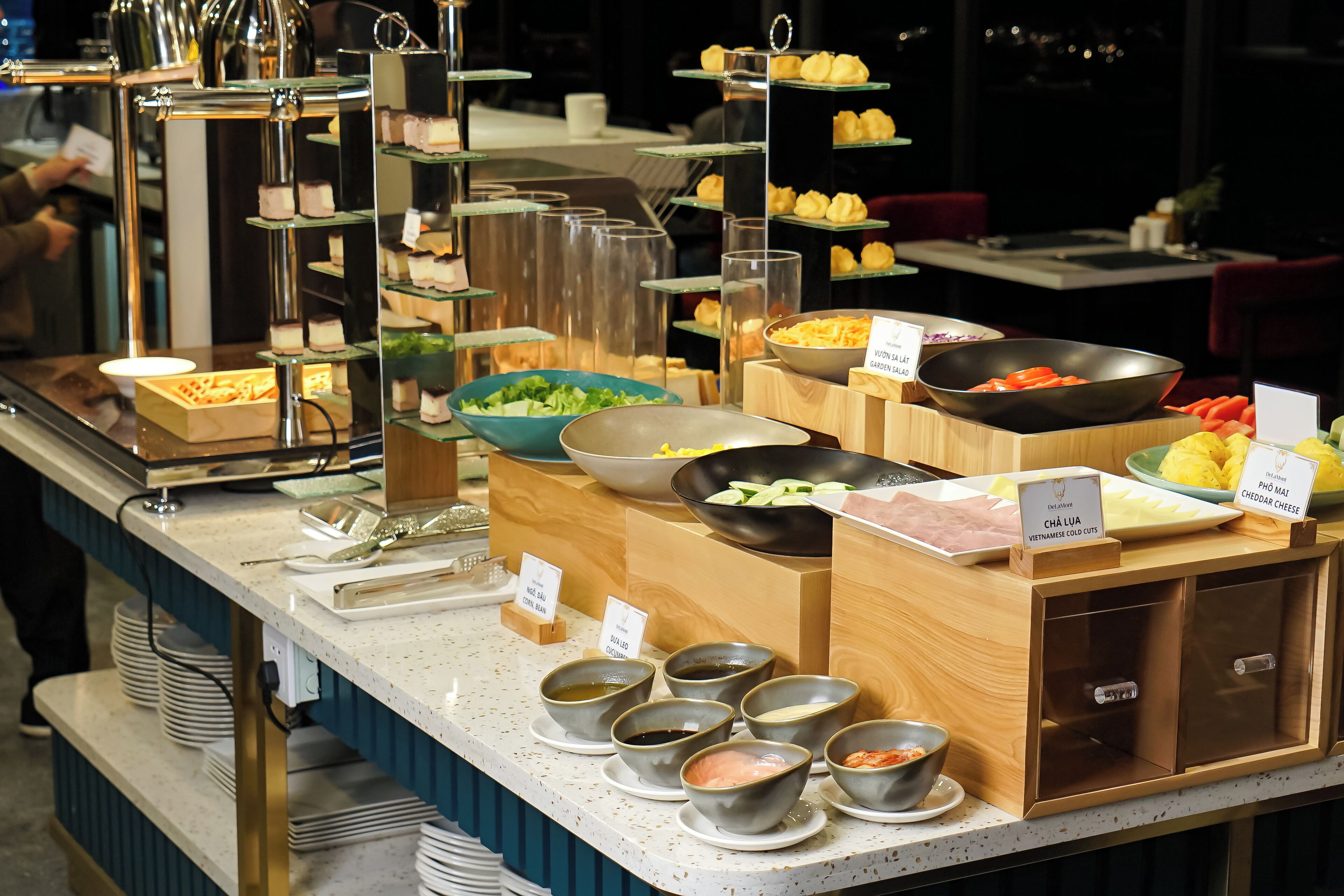 Uma área de buffet com diversas opções de comida, incluindo charcutaria, saladas e molhos.