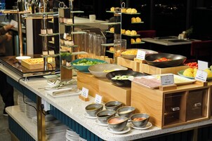 Uma área de buffet com diversas opções de comida, incluindo charcutaria, saladas e molhos.