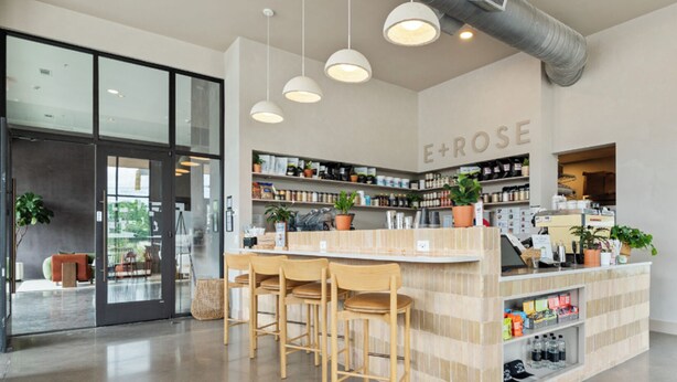 Interior moderno de café com área de bar, assentos e diversos produtos nas prateleiras.