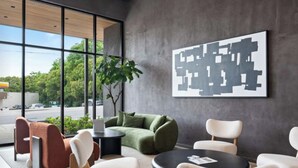 Um interior moderno com um sofá verde, poltronas brancas e uma mesa redonda. Uma grande pintura abstrata está na parede, e há uma planta no canto.